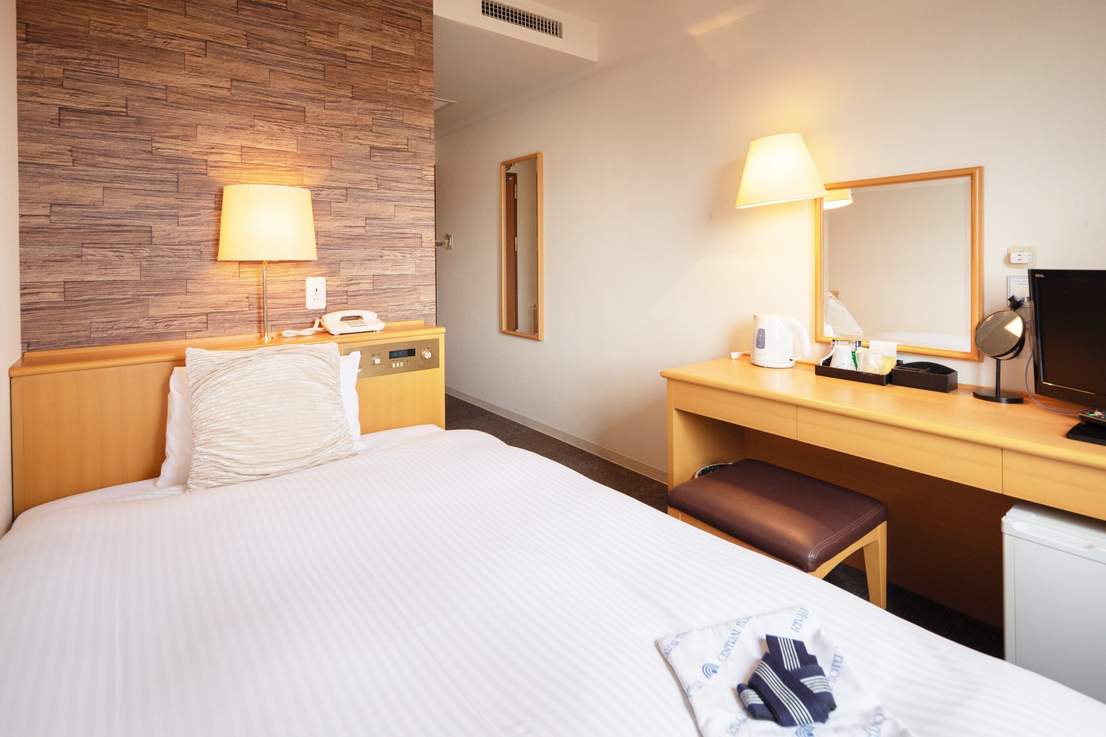 Quarto de hotel com cama, escrivaninha com computador, telefone e espelho.