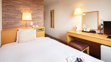 Quarto de hotel com cama, escrivaninha com computador, telefone e espelho.
