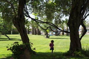 Uma criança brincando em um parque com árvores grandes e uma área gramada.