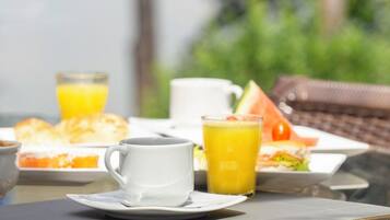 Mesa de café da manhã com uma xícara, um copo de suco de laranja e um prato com comida e uma fatia de melancia.