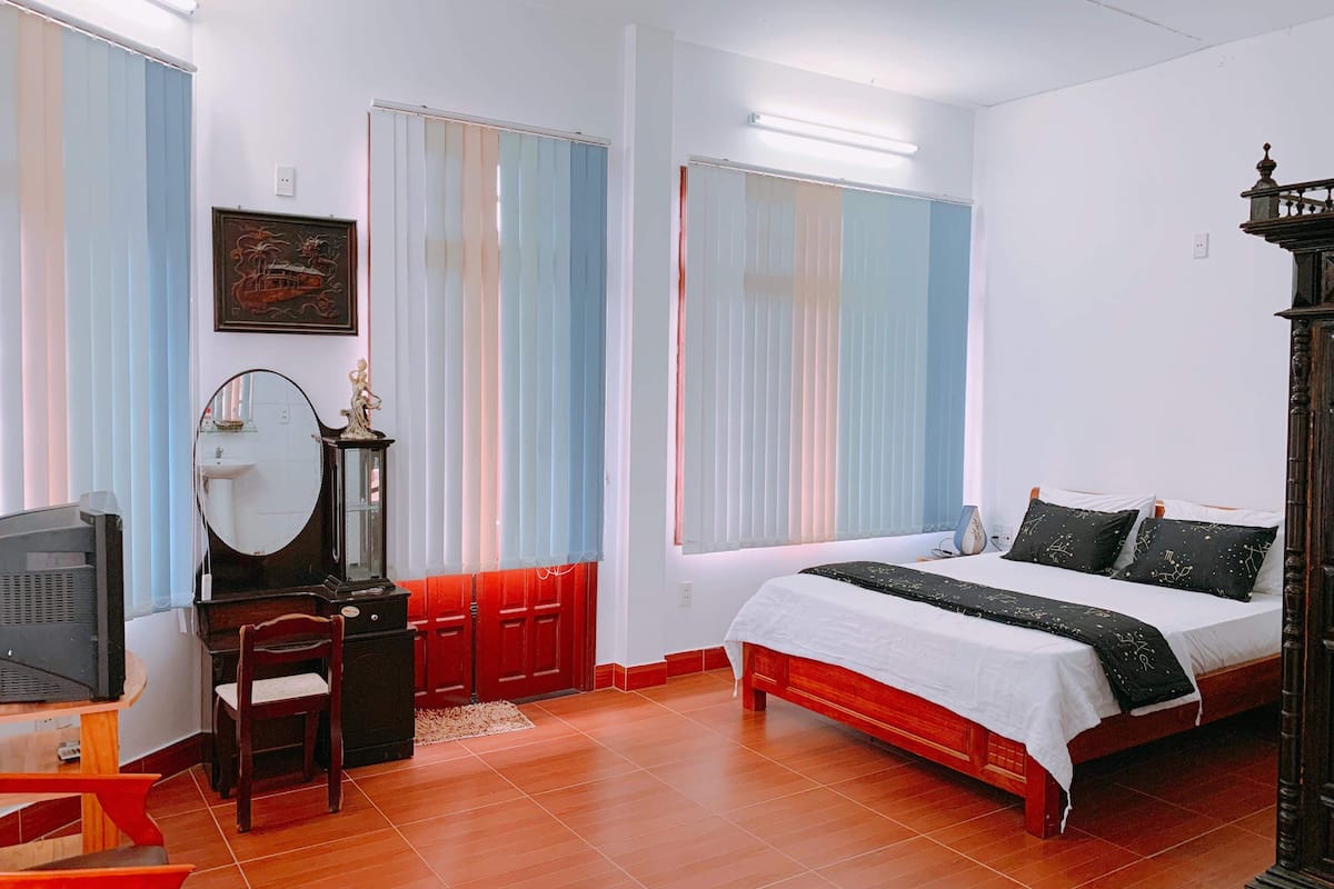 Quarto com cama, escrivaninha com computador, cadeira, cômoda e janela com cortinas.