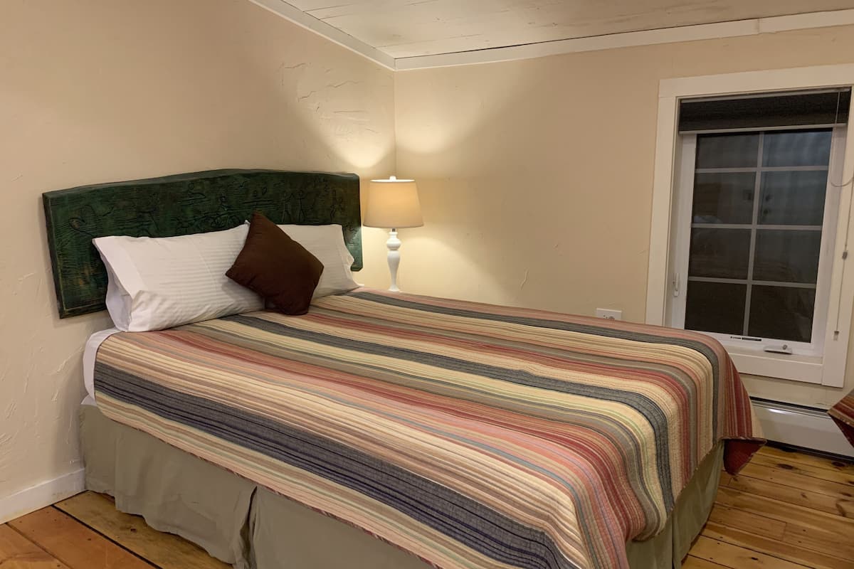 Quarto com cama, cabeceira, abajur e janela.