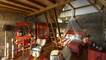 Quarto rústico com parede de pedra, vigas de madeira, cama com dossel, móveis de vime e uma escada.