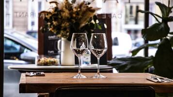 Uma mesa com dois copos de vinho vazios e um suporte para menu, com um arranjo floral ao fundo.