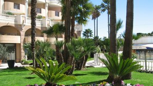 Um pátio de hotel com palmeiras, um jardim de flores e um edifício com varandas.