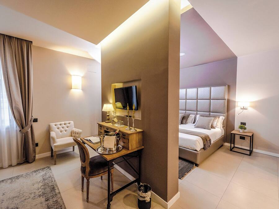 Quarto de hotel com cama, escrivaninha, cadeira, televisão e mesa de cabeceira.
