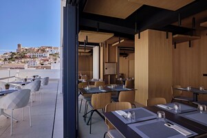 Uma sala de jantar moderna com mesas e cadeiras, vista para a paisagem urbana e decoração em madeira.