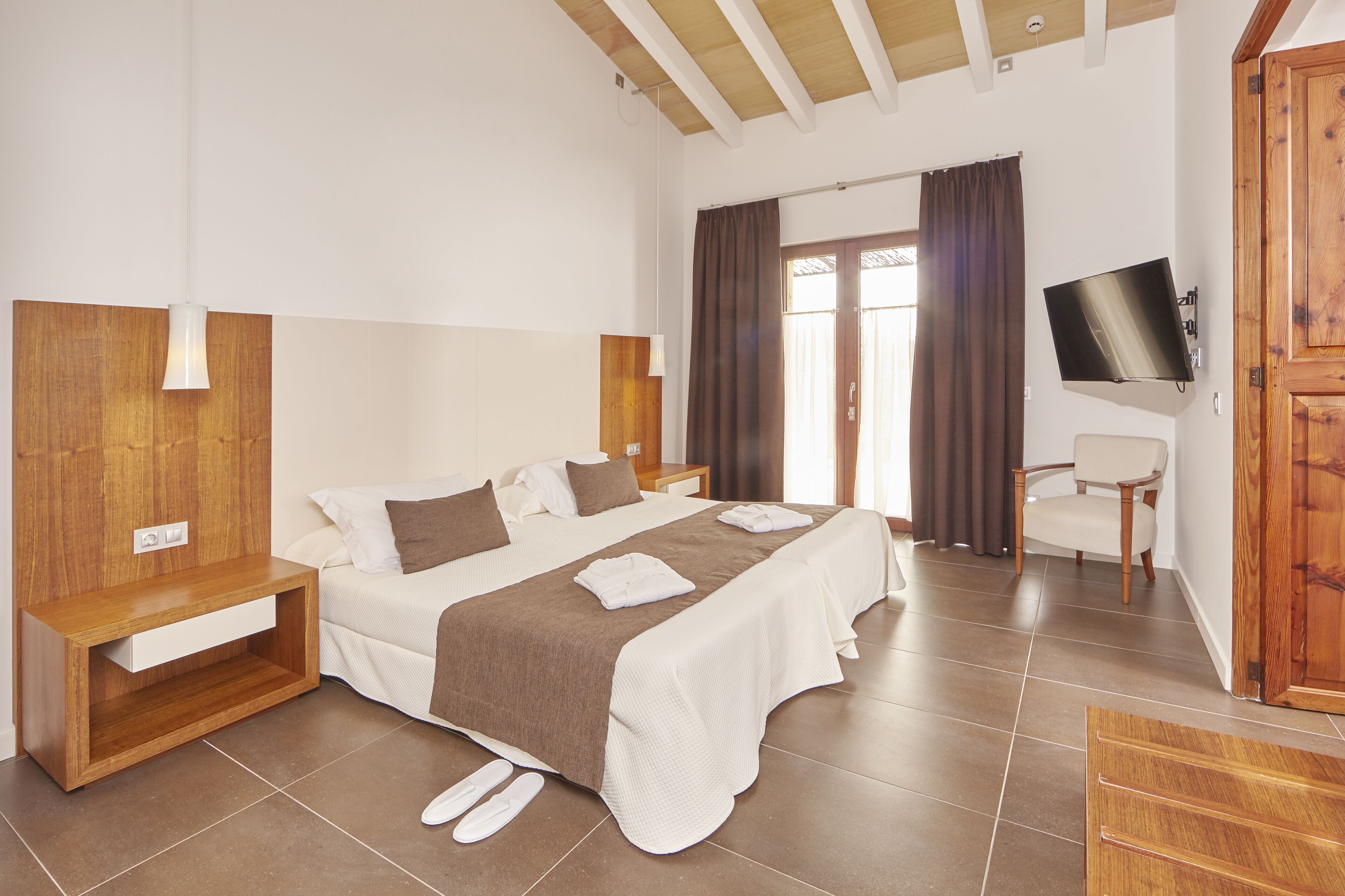 Quarto com uma cama grande, cabeceira de madeira, mesas de cabeceira, televisão, uma cadeira e um guarda-roupa.