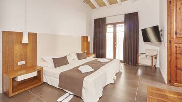 Quarto com uma cama grande, cabeceira de madeira, mesas de cabeceira, televisão, uma cadeira e um guarda-roupa.