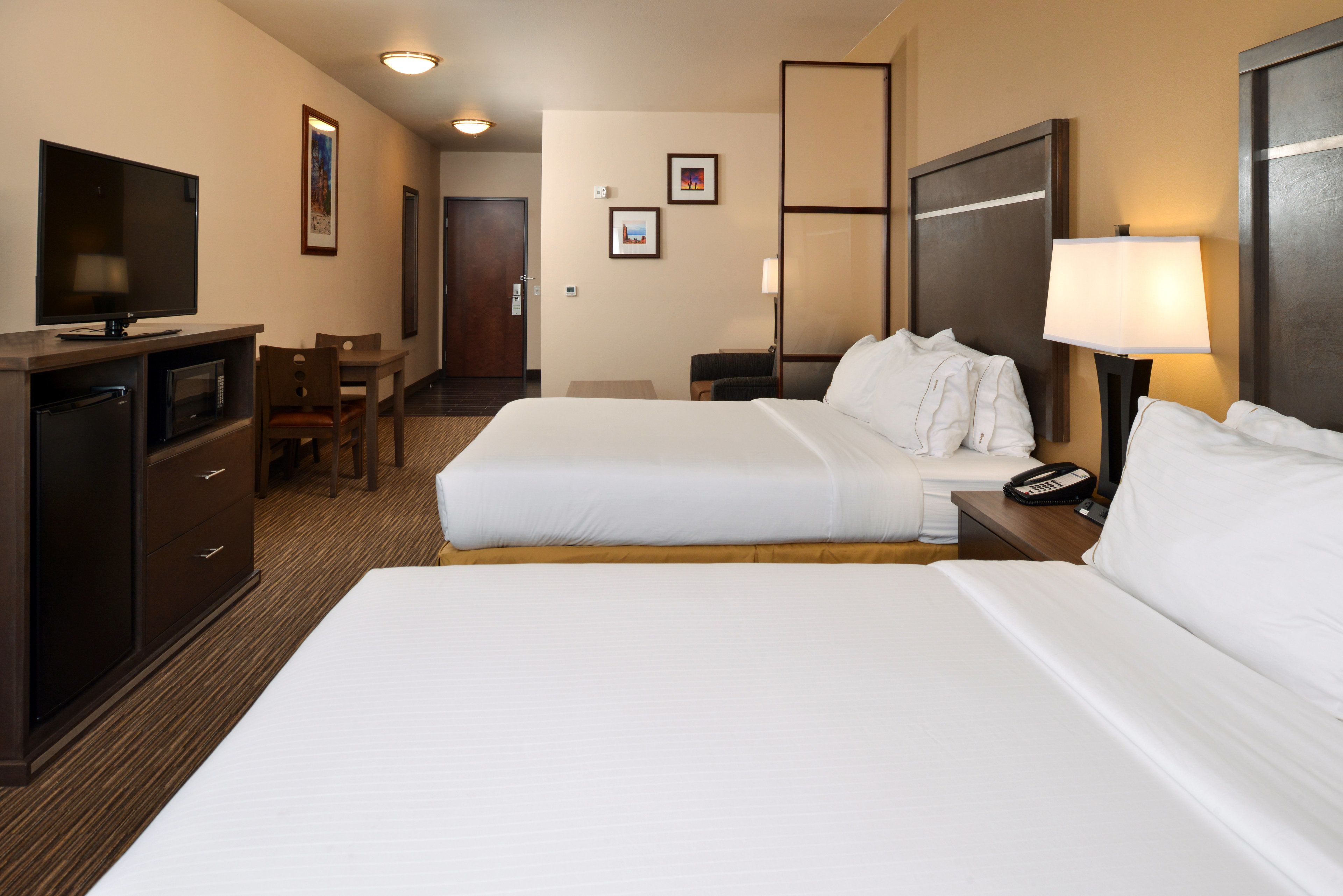Quarto de hotel com duas camas, uma mesa, televisão de tela plana, micro-ondas e uma cadeira.