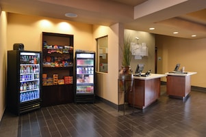 Uma área de recepção de hotel com dois dispensadores de bebidas, um balcão de recepção e um vaso de plantas.