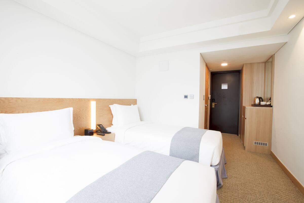 Quarto de hotel com duas camas, uma mesa de cabeceira, uma escrivaninha e um guarda-roupa.