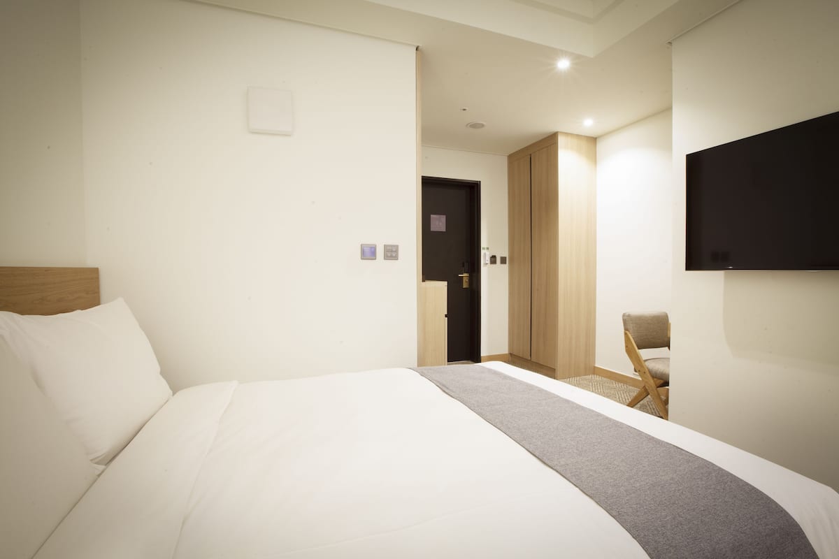 Quarto de hotel com uma cama grande, televisão de tela plana na parede e guarda-roupa de madeira.