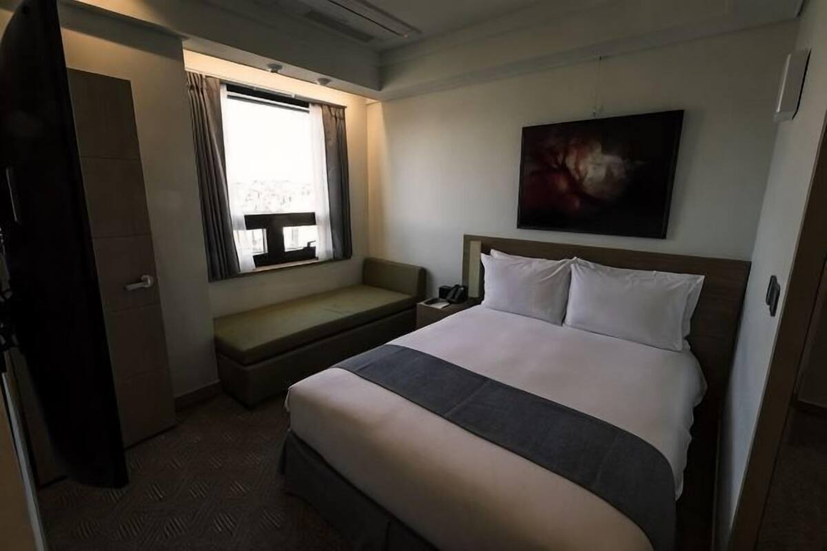 Quarto de hotel com cama, um banco, uma janela e um quadro na parede.