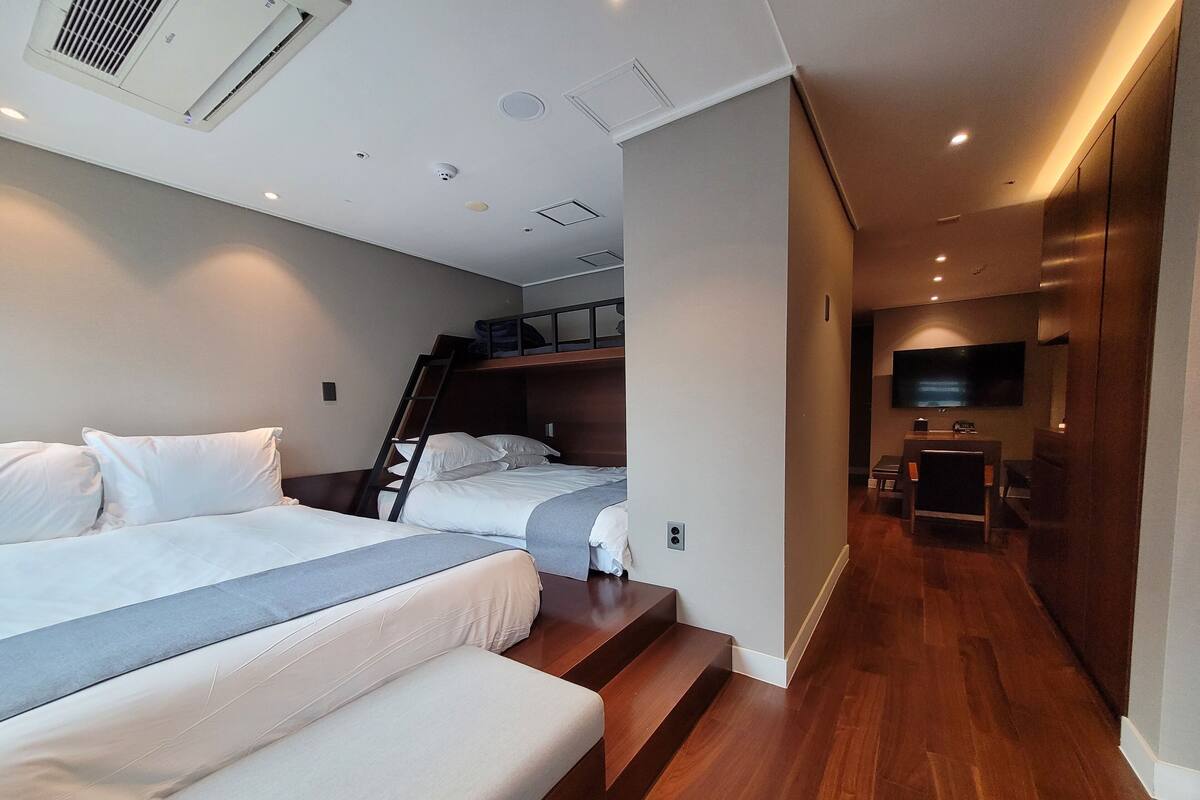 Quarto de hotel moderno com duas camas, televisão e um pequeno espaço de trabalho.
