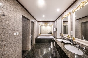 Casa de banho moderna com paredes de granito, chão de mármore preto, duas pias e um espelho grande com detalhes dourados.