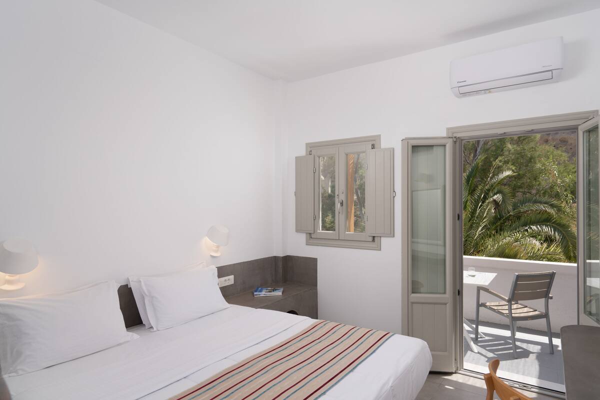 Quarto com cama, mesa de cabeceira, janela com cortinas e ar condicionado.