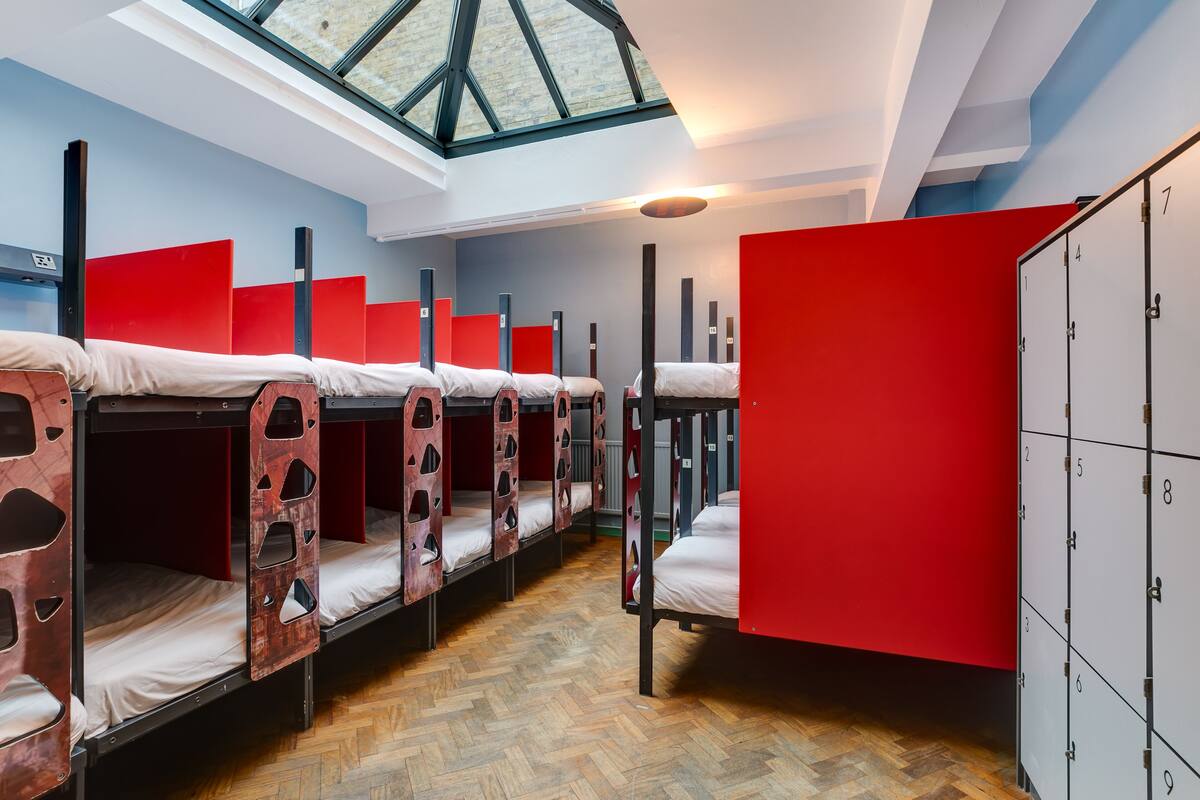 Quarto em dormitório com beliches, claraboia e parede divisória vermelha.