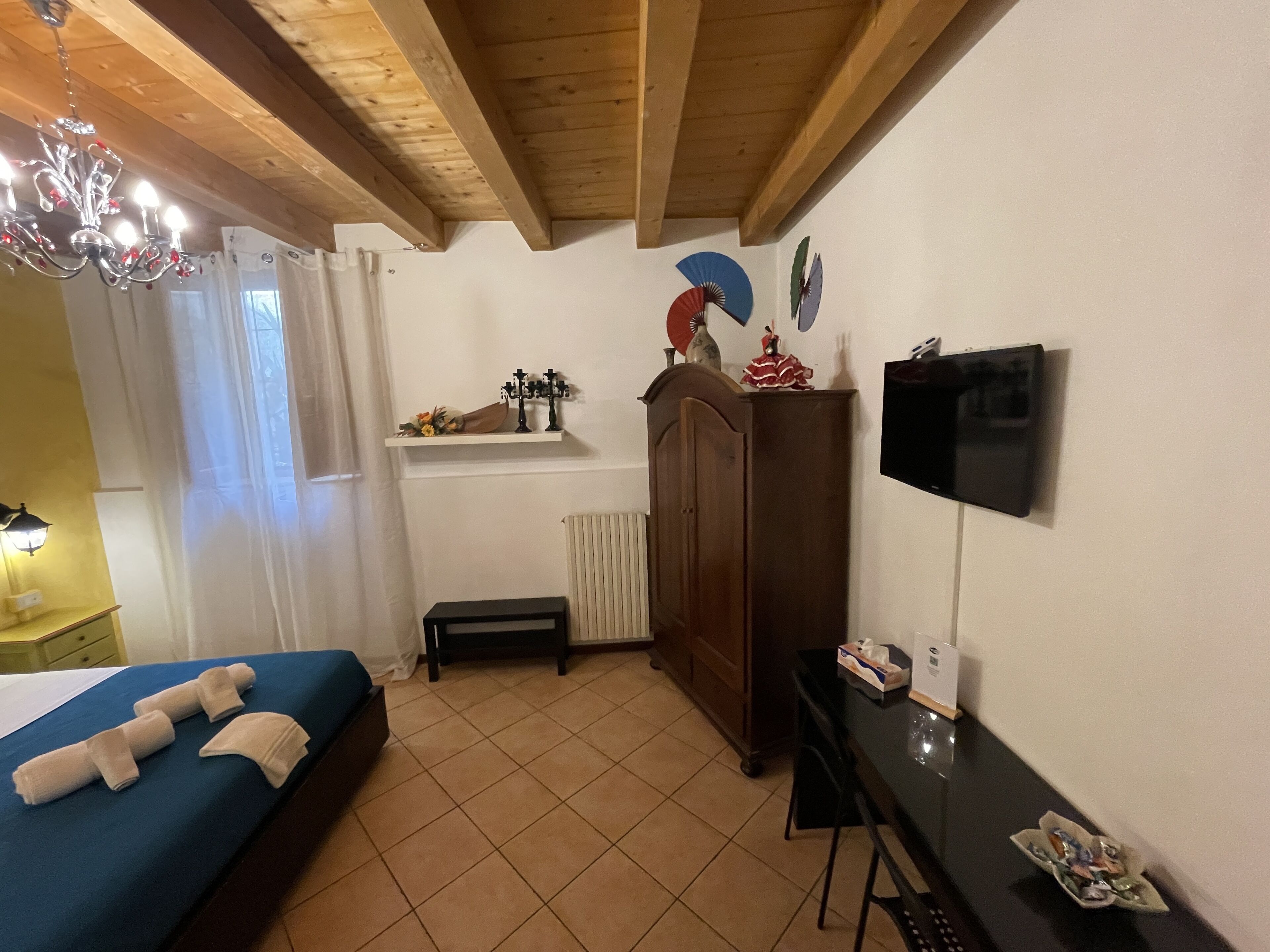 Quarto com cama, escrivaninha, televisão, radiador e teto de madeira.
