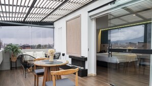 Uma zona de refeições moderna com uma mesa redonda e cadeiras de madeira, uma cadeira preta, uma pequena planta em vaso e vista através de uma porta de vidro para uma área de estar ao ar livre.