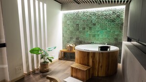 Uma casa de banho moderna com uma banheira de madeira, uma parede em mosaico verde e uma planta em vaso.