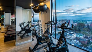 Uma academia com equipamentos de ginástica, amplas janelas e vista para a cidade.