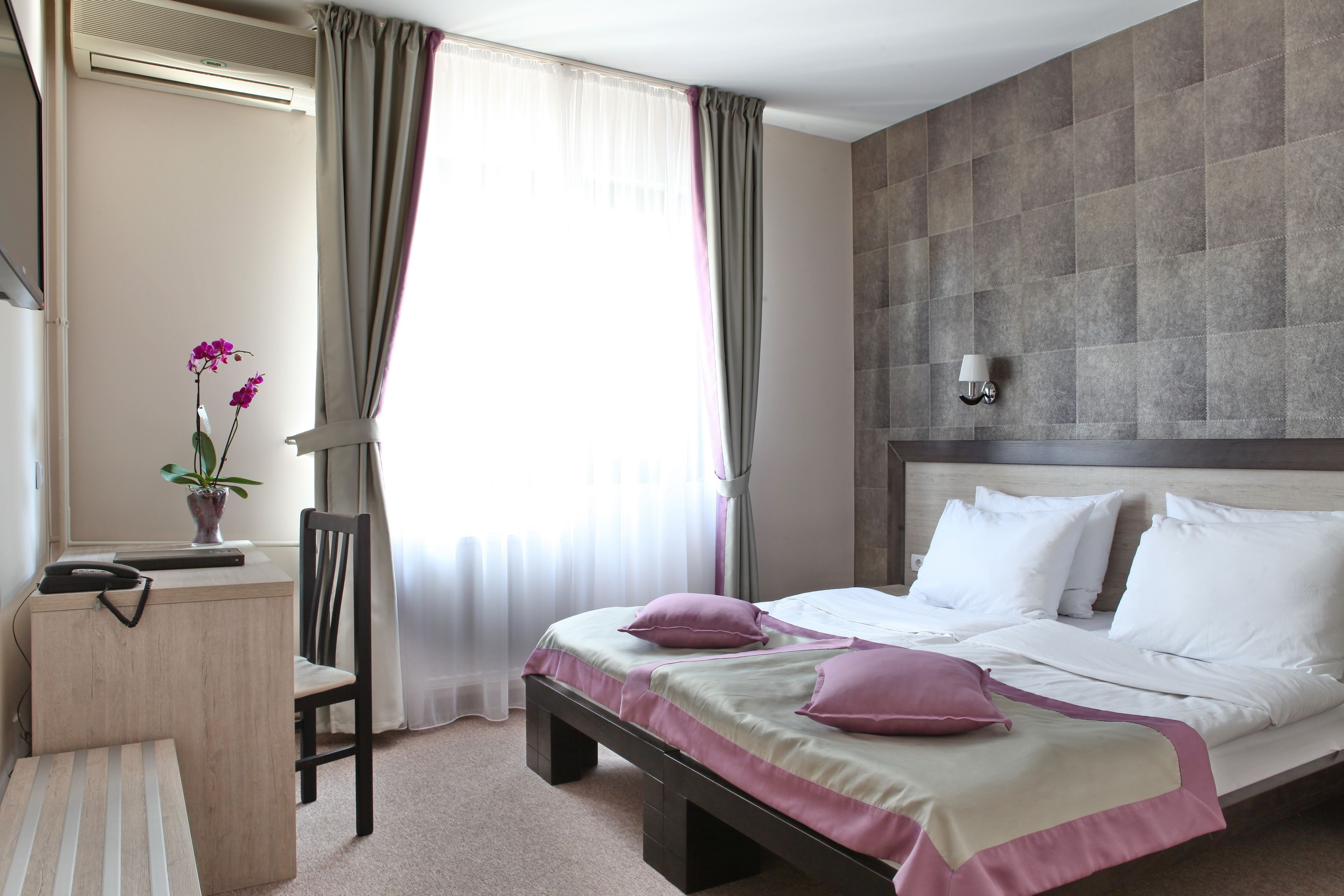 Quarto de hotel com cama, escrivaninha, cadeira e janela com cortinas.