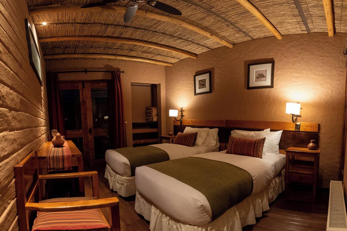 Quarto de hotel acolhedor com duas camas, cabeceiras de madeira e teto de colmo.