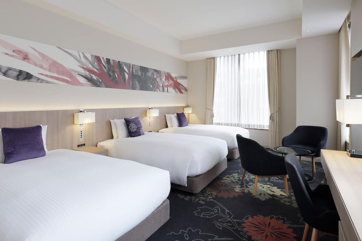 Quarto de hotel com duas camas, uma escrivaninha, uma cadeira e um quadro abstrato grande na parede.