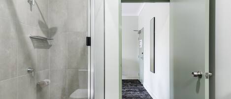 Uma casa de banho moderna com chuveiro de vidro, sanita e base de chuveiro.