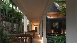 Um corredor com bancos e mesas de madeira, rodeado por plantas tropicais exuberantes.