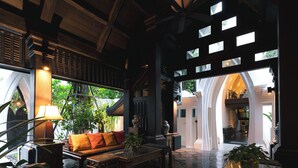 Um hall amplo com teto de madeira, um sofá com almofadas, uma mesa e um vaso de planta.