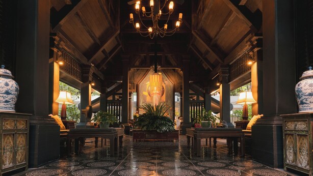Um hall com um candelabro, vigas de madeira e um vaso grande sobre uma mesa.