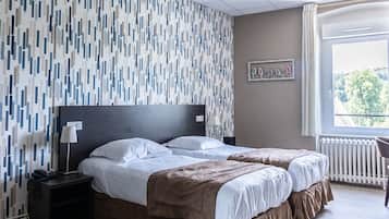 Quarto de hotel moderno com uma cama grande, uma mesinha de cabeceira com abajur, um relógio de parede e uma janela com vista para árvores.