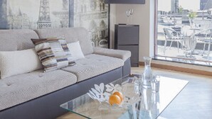 Uma sala de estar moderna com uma grande janela, um sofá, uma mesa de centro de vidro e uma televisão de tela plana.