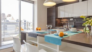Uma cozinha moderna com uma ilha grande, armários brancos e vista para a cidade através de amplas janelas.