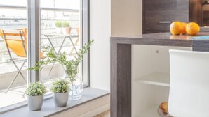 Cozinha moderna com uma janela grande, área de jantar com uma cadeira branca e uma pequena mesa com laranjas.