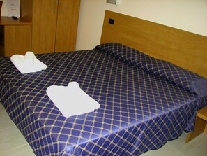 Cama bem arrumada com colcha quadriculada azul e amarela, duas almofadas brancas e cabeceira de madeira.