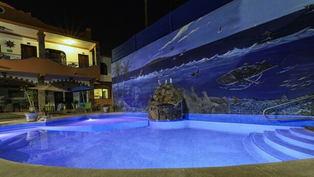 Piscina com um mural de vida marinha e oceano, rodeada por um edifício com varandas e área externa para sentar.