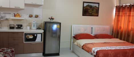 Quarto de hotel compacto com cozinha compacta, uma cama com roupa de cama vermelha e uma pequena janela com cortinas.