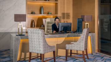 Bancada de recepção com computador, duas poltronas estofadas e piso de mármore.