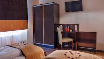Quarto de hotel com duas camas, um guarda-roupa, uma secretária com cadeira, televisão e janela com cortinas.