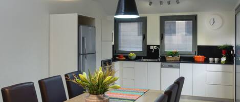Cozinha moderna com armários brancos, mesa de jantar de madeira e luminária pendente preta.