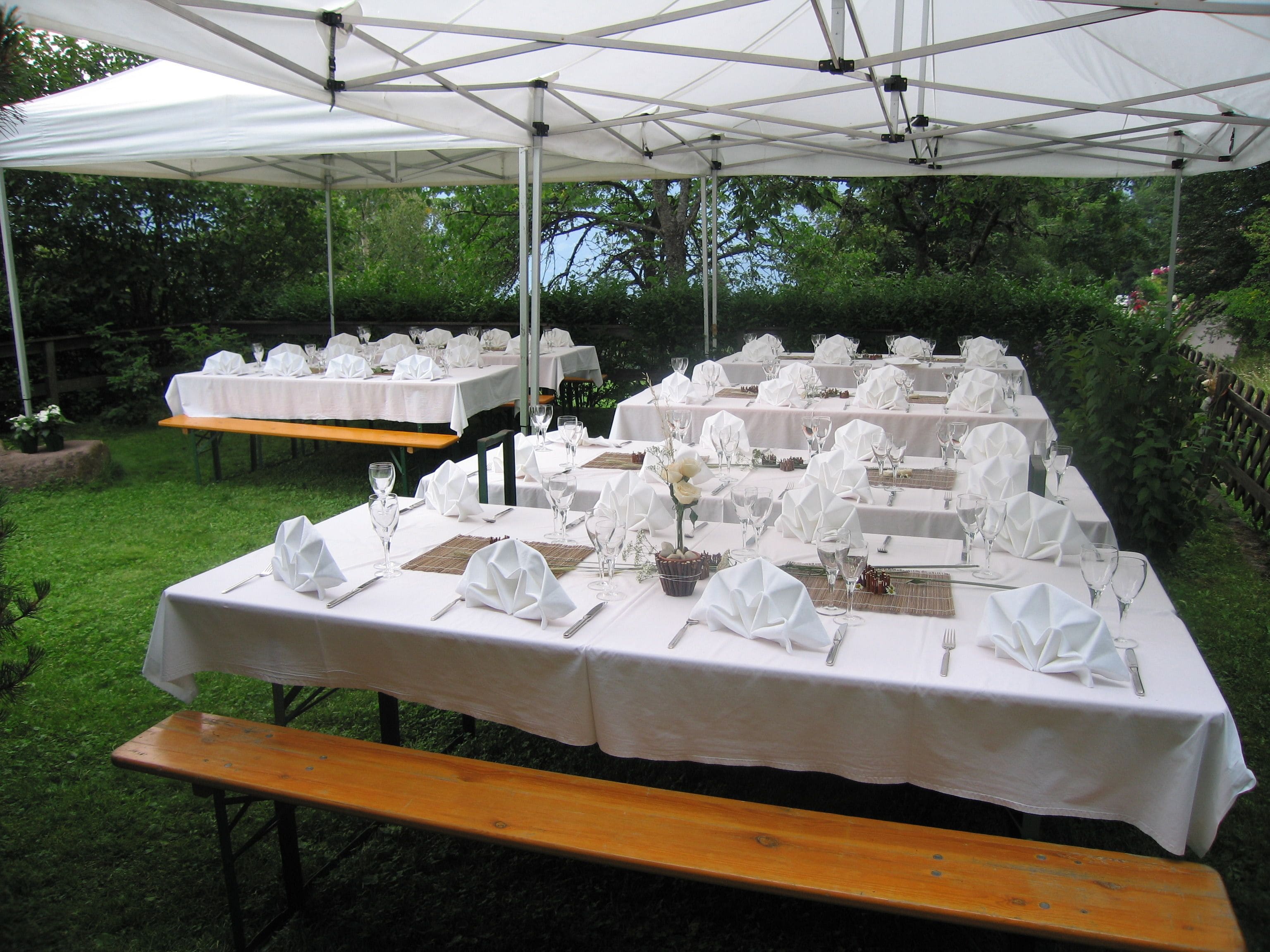 Espaço para eventos ao ar livre com várias mesas preparadas para refeições, coberto por um toldo branco.
