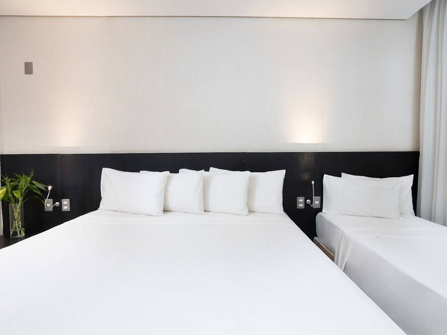 Quarto de hotel moderno com uma cama grande, cabeceira preta e mesa de cabeceira com abajur.