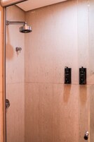 Área de chuveiro com chuveiro manual, painel de controle e duas embalagens de shampoo fixadas na parede.