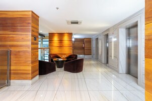 Um lobby moderno com painéis de madeira, piso de mármore e uma área de estar com duas cadeiras e uma mesa.