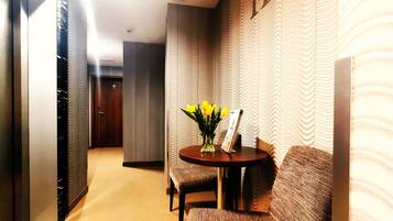Um corredor de hotel com uma mesa redonda, um vaso com flores amarelas e um sofá.