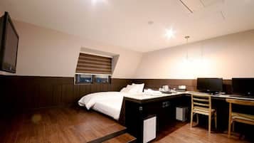 Quarto de hotel com cama, escrivaninha, dois monitores, uma cadeira e um armário pequeno.