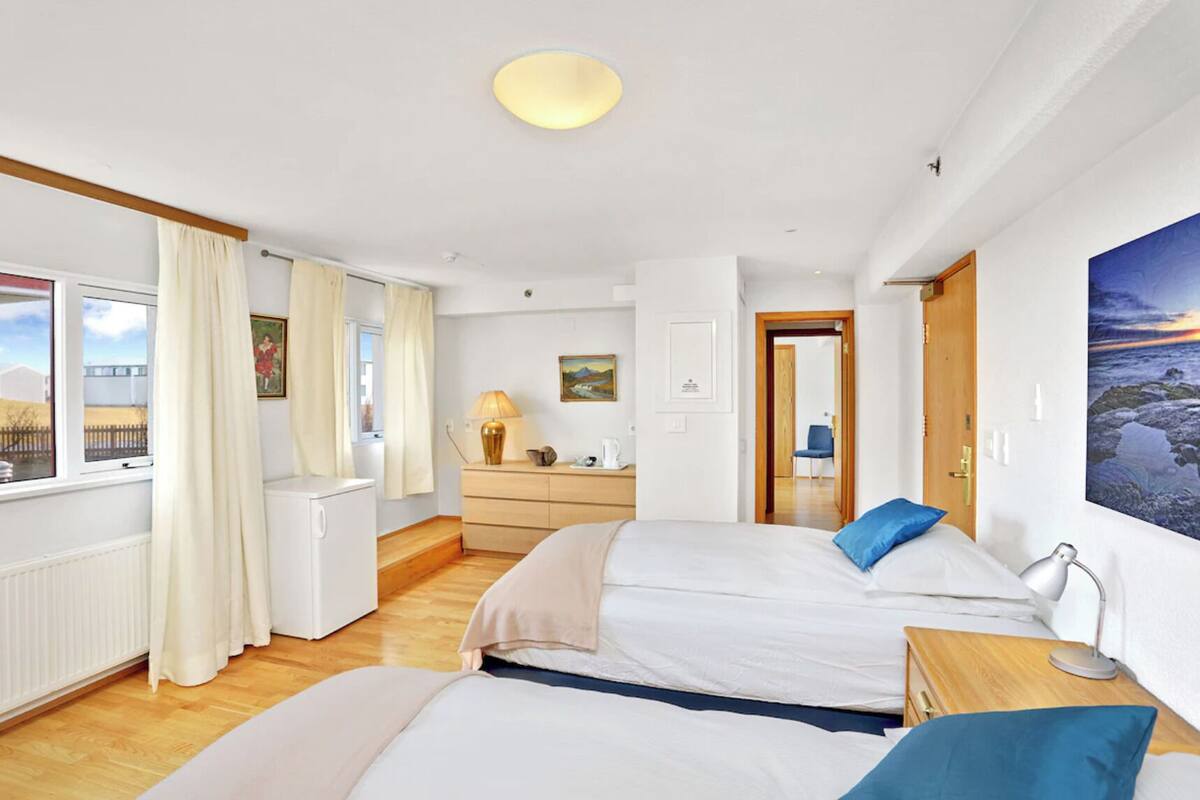 Quarto de hotel com duas camas, penteadeira de madeira, escrivaninha, abajur e um quadro na parede.